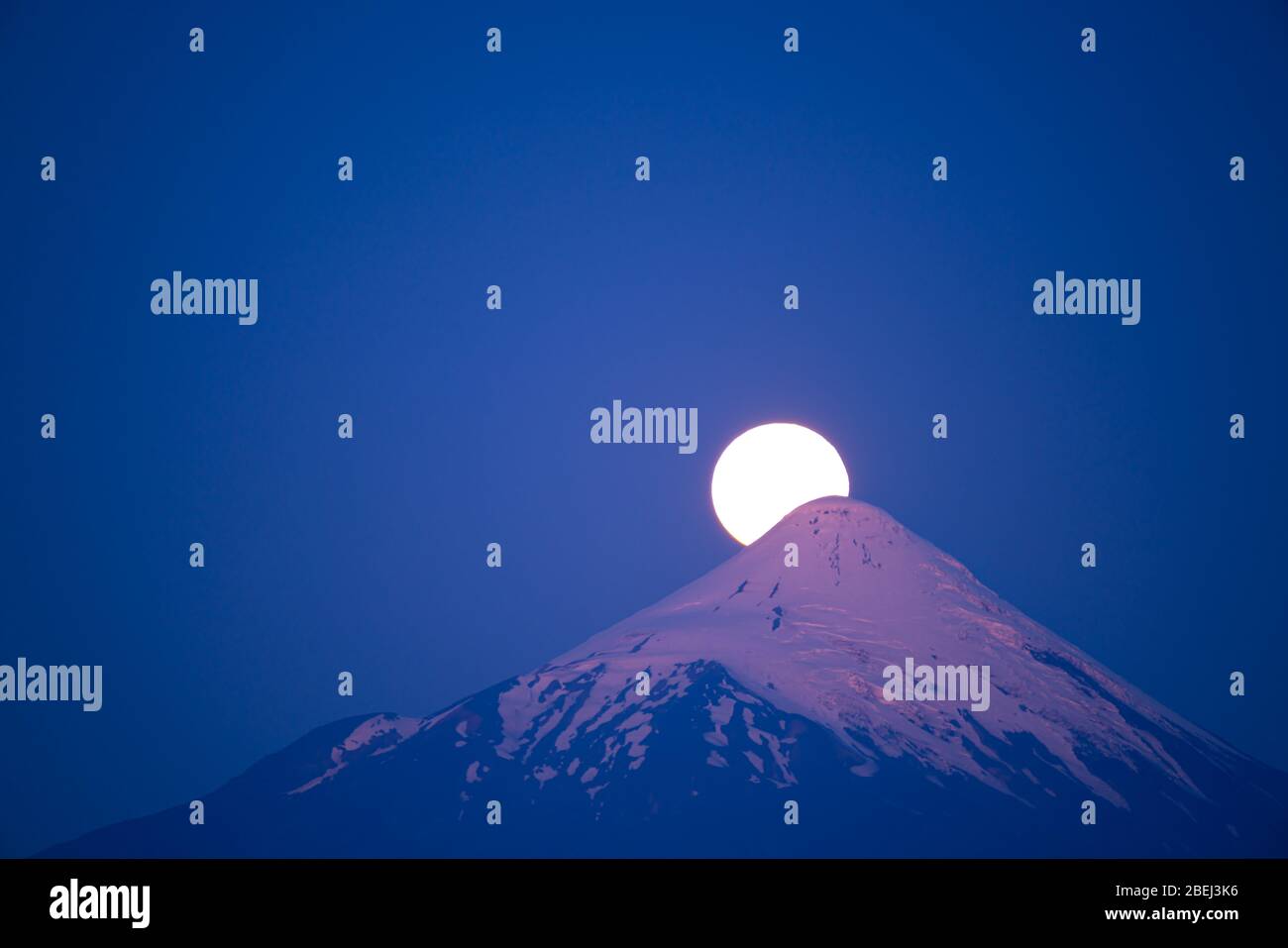 full moon rising behind the top of the Osorno volcano after sunset with ...