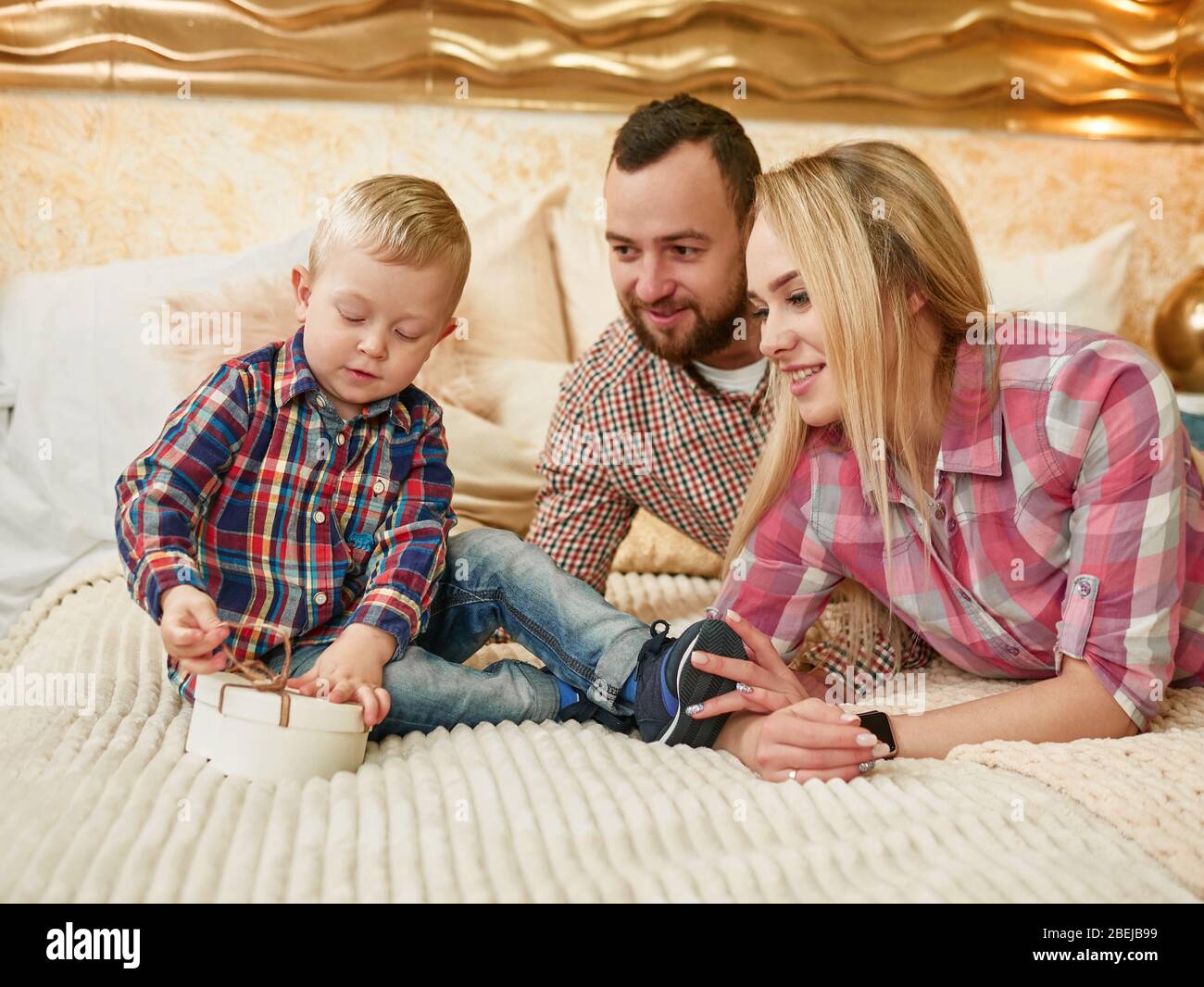 little boy opens a gift with parents, smiling kid, happy family concept ...