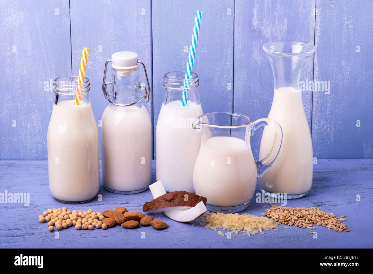 types of vegetable and organic milk in glass containers on a light blue ...