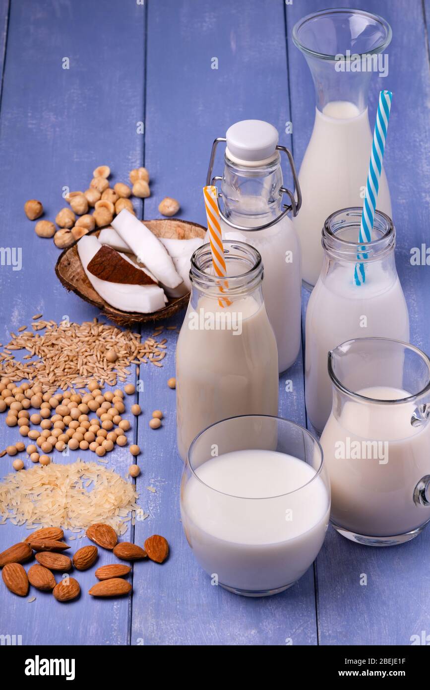 types of vegetable and organic milk in glass containers on a light blue ...