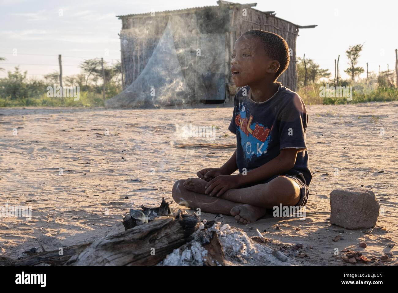 A young Ju/hoansi boy sits by the fire at dawn in the village of Deng ...