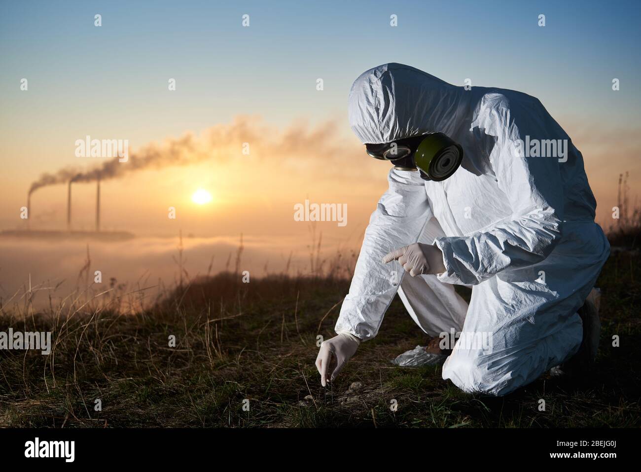 Scientist in protective suit and gas mask taking soil sample at power ...
