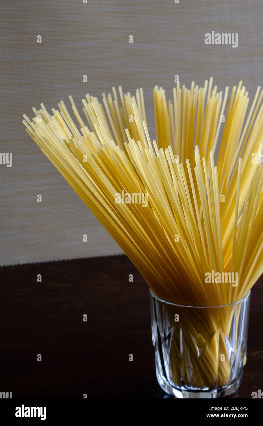 Spaghetti in a glass cup on a brown wooden table. A bunch of spaghetti ...