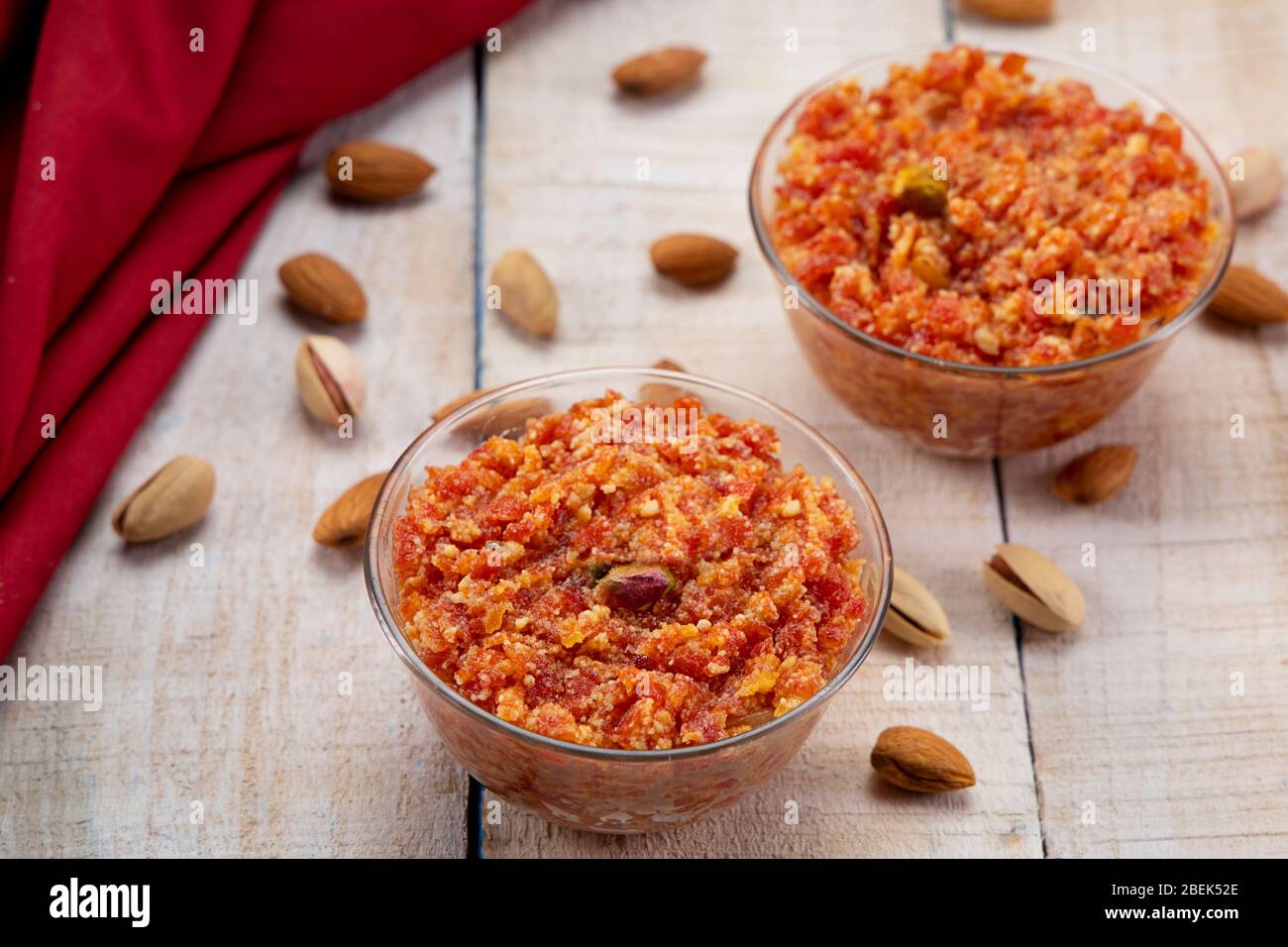 Two bowls of gajar ka halwa kept on a wooden table with dry fruits ...