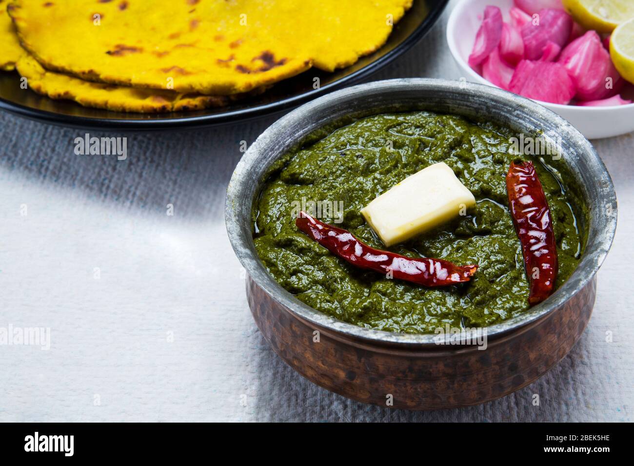 Sarso ka saag and makki ki roti kept on a table with pickled onions ...