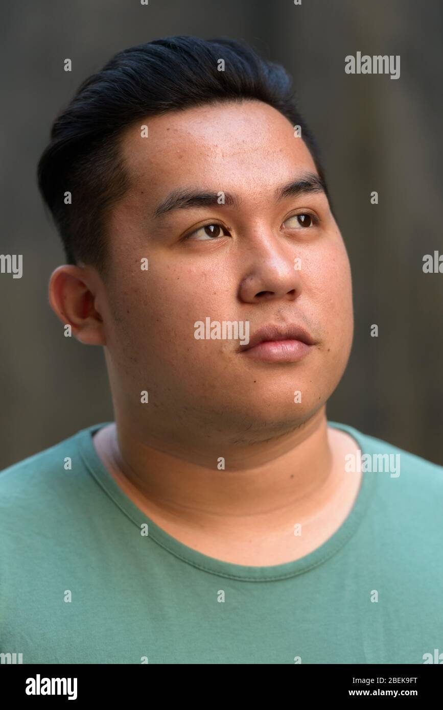 Face of young handsome overweight Asian man thinking outdoors Stock ...
