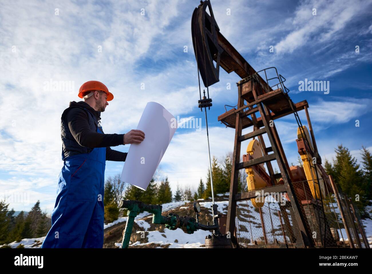 Petroleum engineer in blue uniform and orange helmet standing in oil ...
