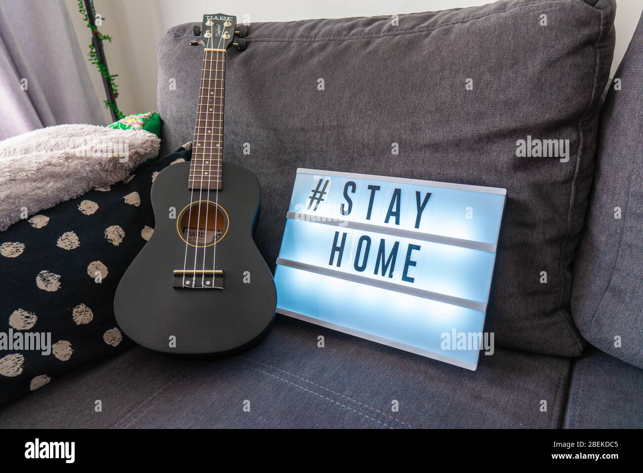 Coronavirus home lightbox sign with hashtag message #STAYHOME glowing on home sofa with cozy ...