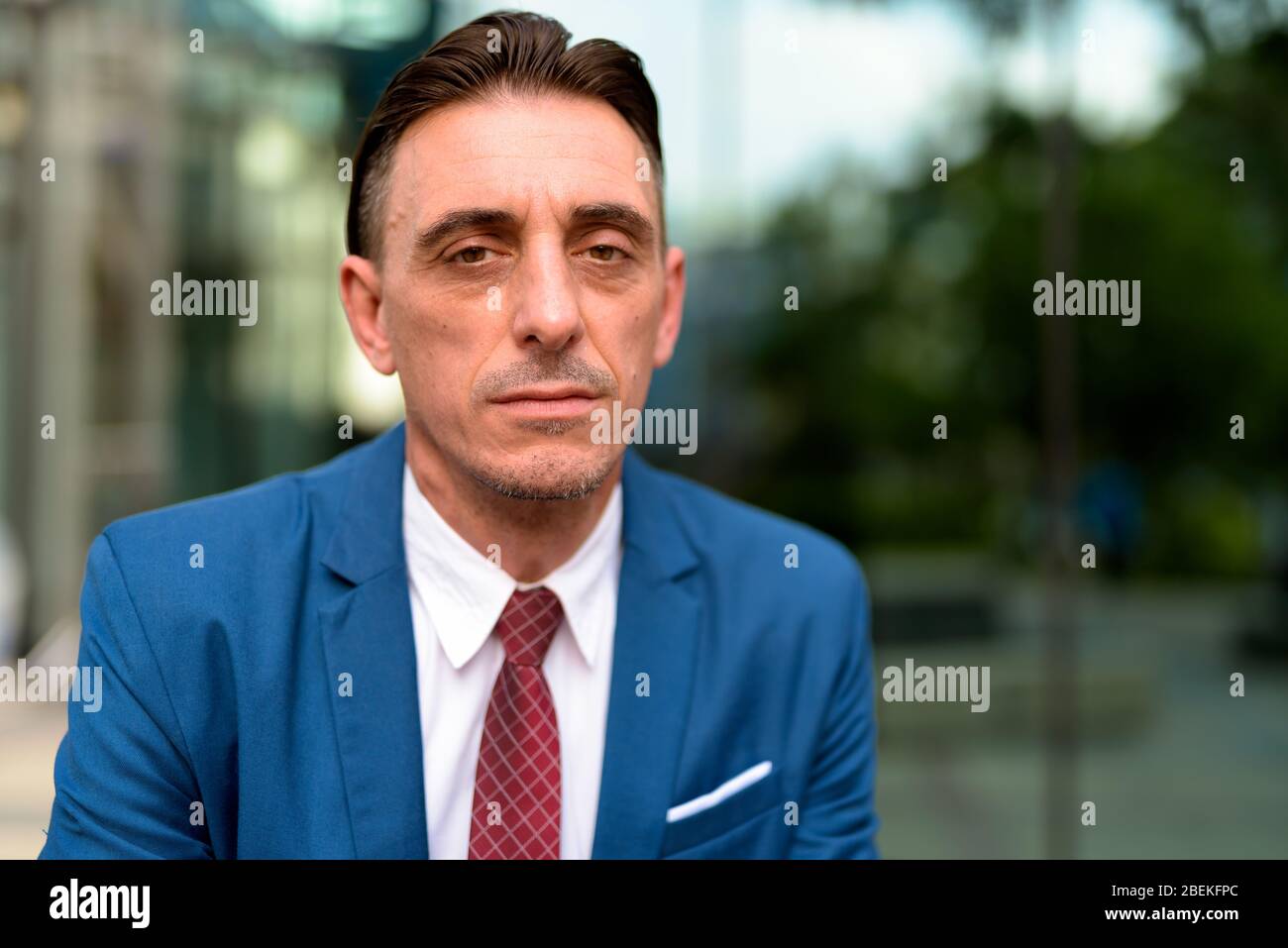 Mature handsome Italian businessman relaxing outside of the building ...