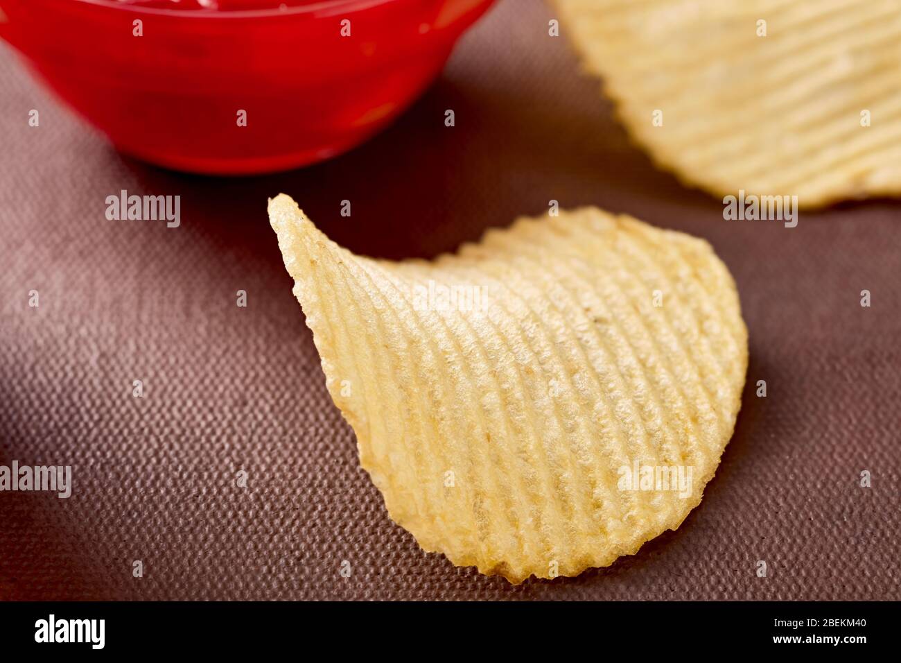 One potato chip on brown table against chili salsa sauce and potato ...
