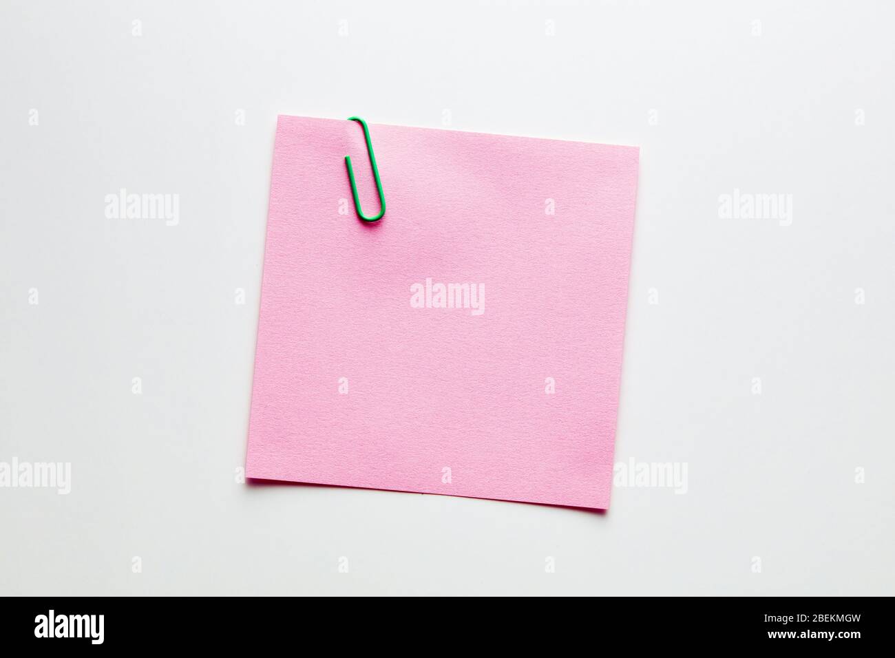 Blank pink note paper or notepad with a green paper clip on white ...