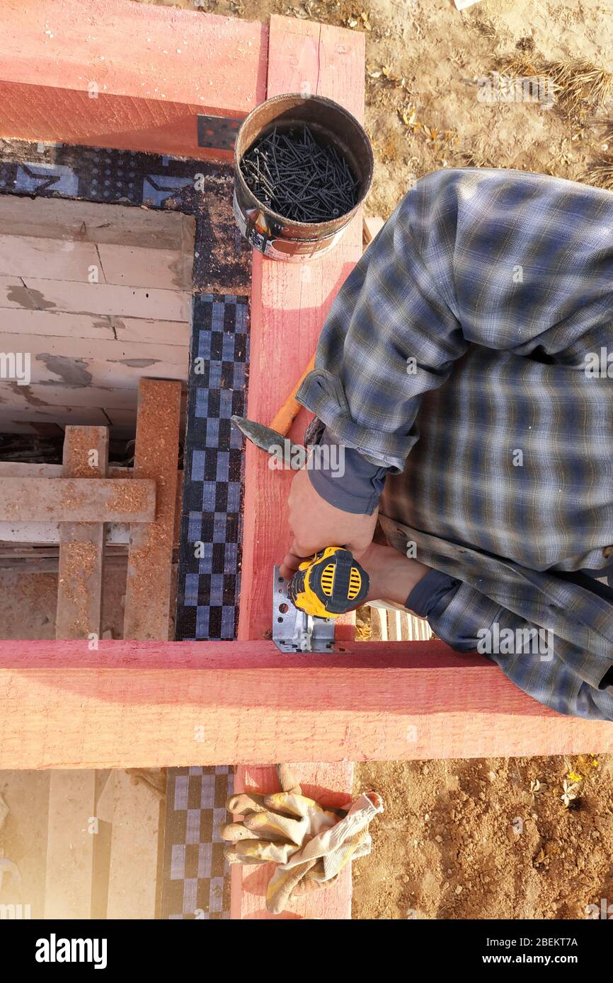 In the roof rafters the worker screws the screws into the screwdriver ...