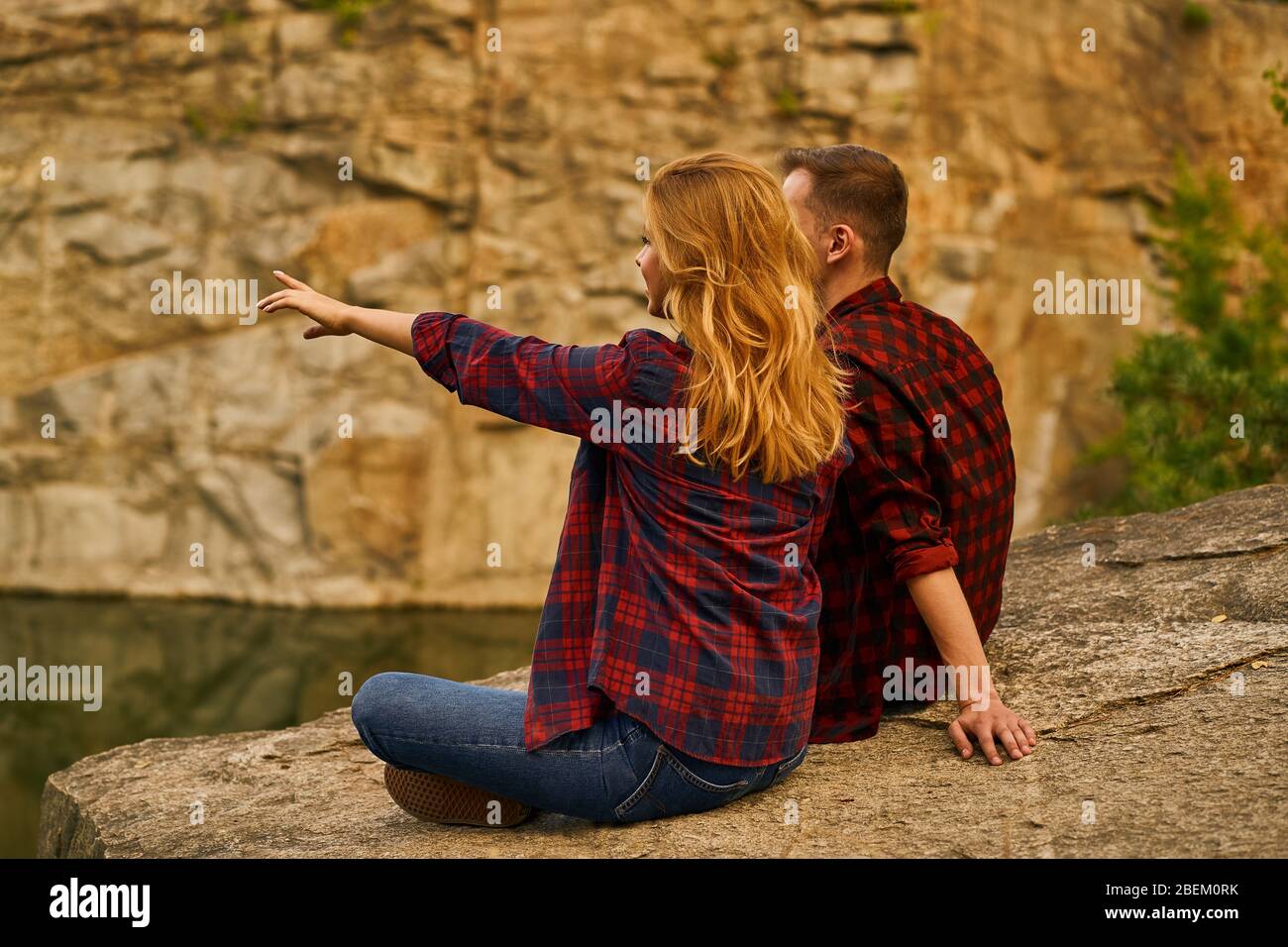 Cute couple sits at rock near the lake at forest and canyon background ...