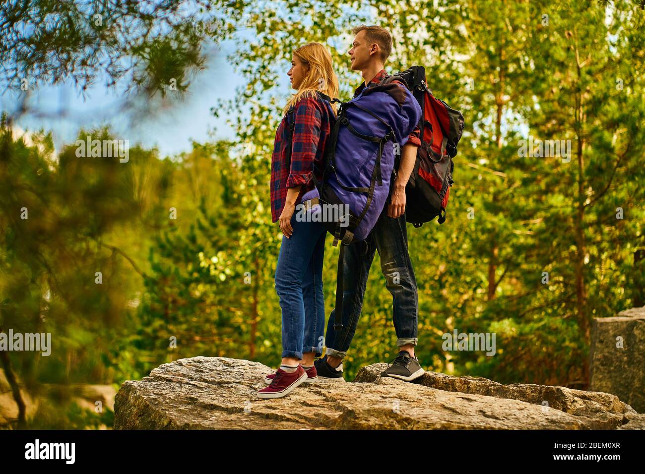 Cute couple with backpacks stand at rock near the lake at forest and ...