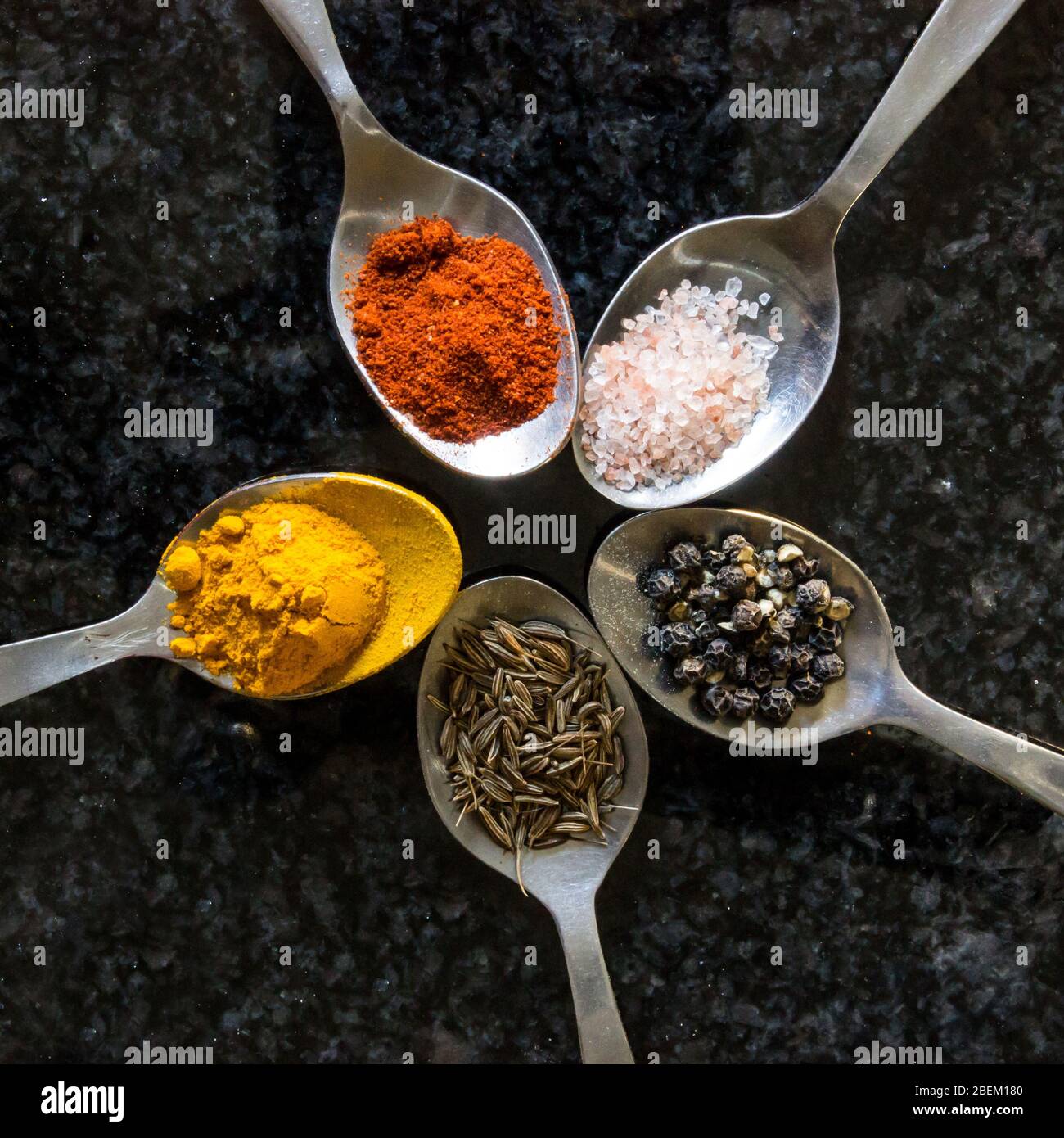 Five stainless steel teaspoons, filled with various types of spices, in ...