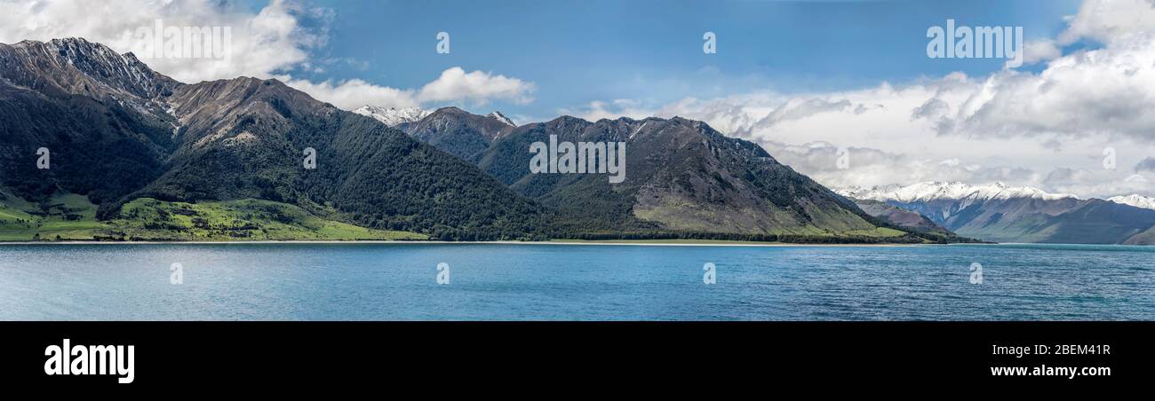 landscape of Hawea Alpine lake with green shores and snow capped ...