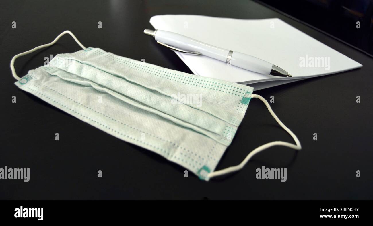 Paper notepad for notes next to pen and a surgical/medical face mask ...