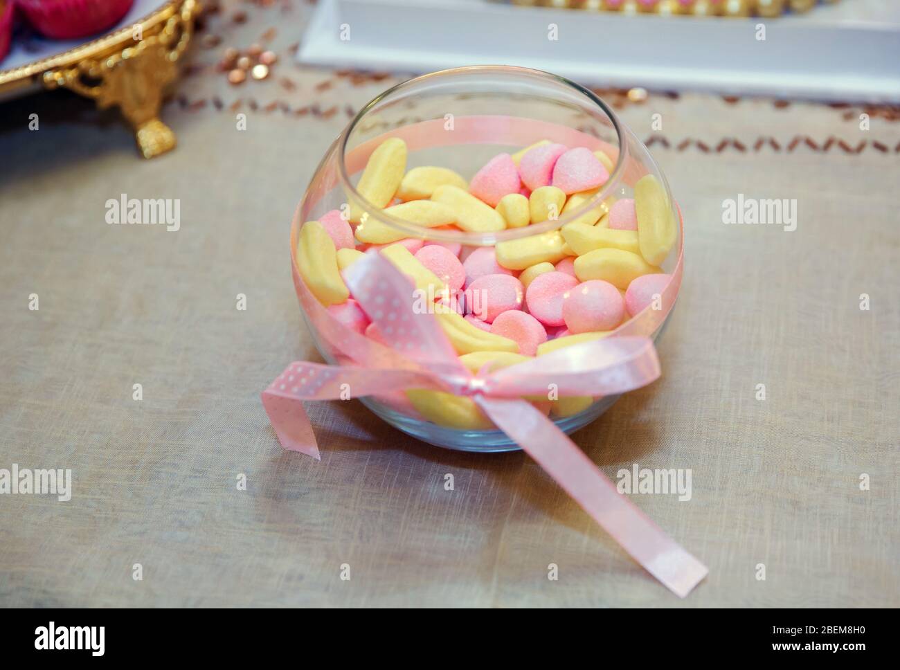 Pink and yellow candies in glass vase on white background ...