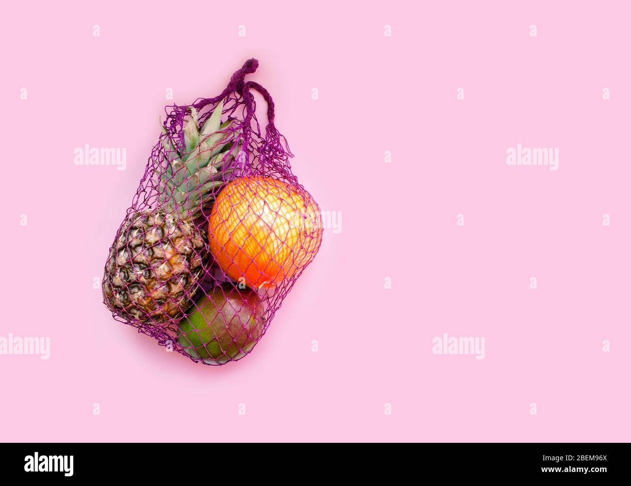 Tropical fruits in a string string bag. pineapple, mango, pomelo. Pink ...