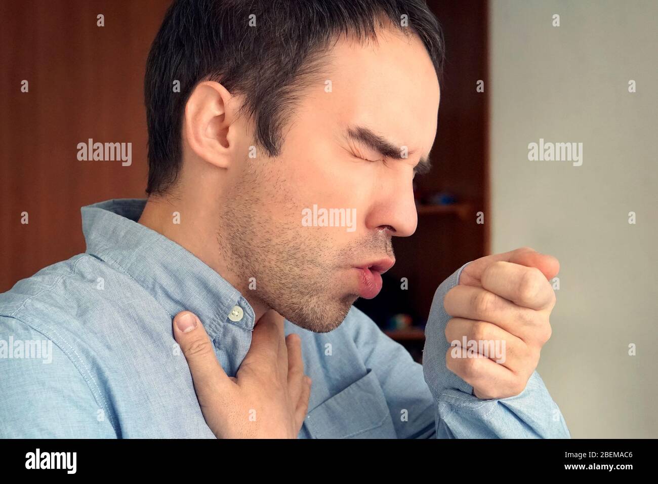 A young man sneezing into his elbow. Coughing into clothes as a means ...