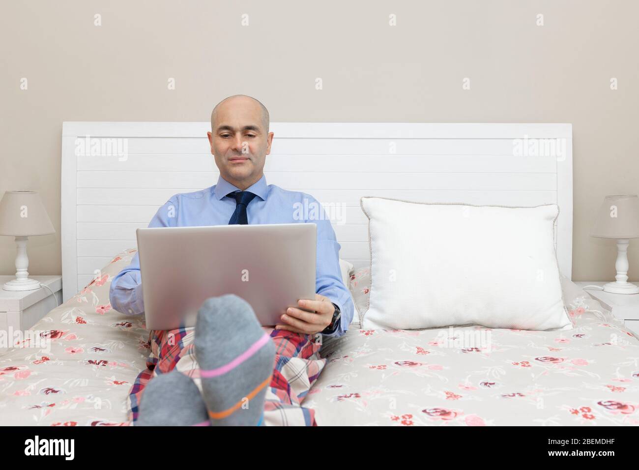 Man working with a laptop in a bed wearing a shirt and tie and pajama ...