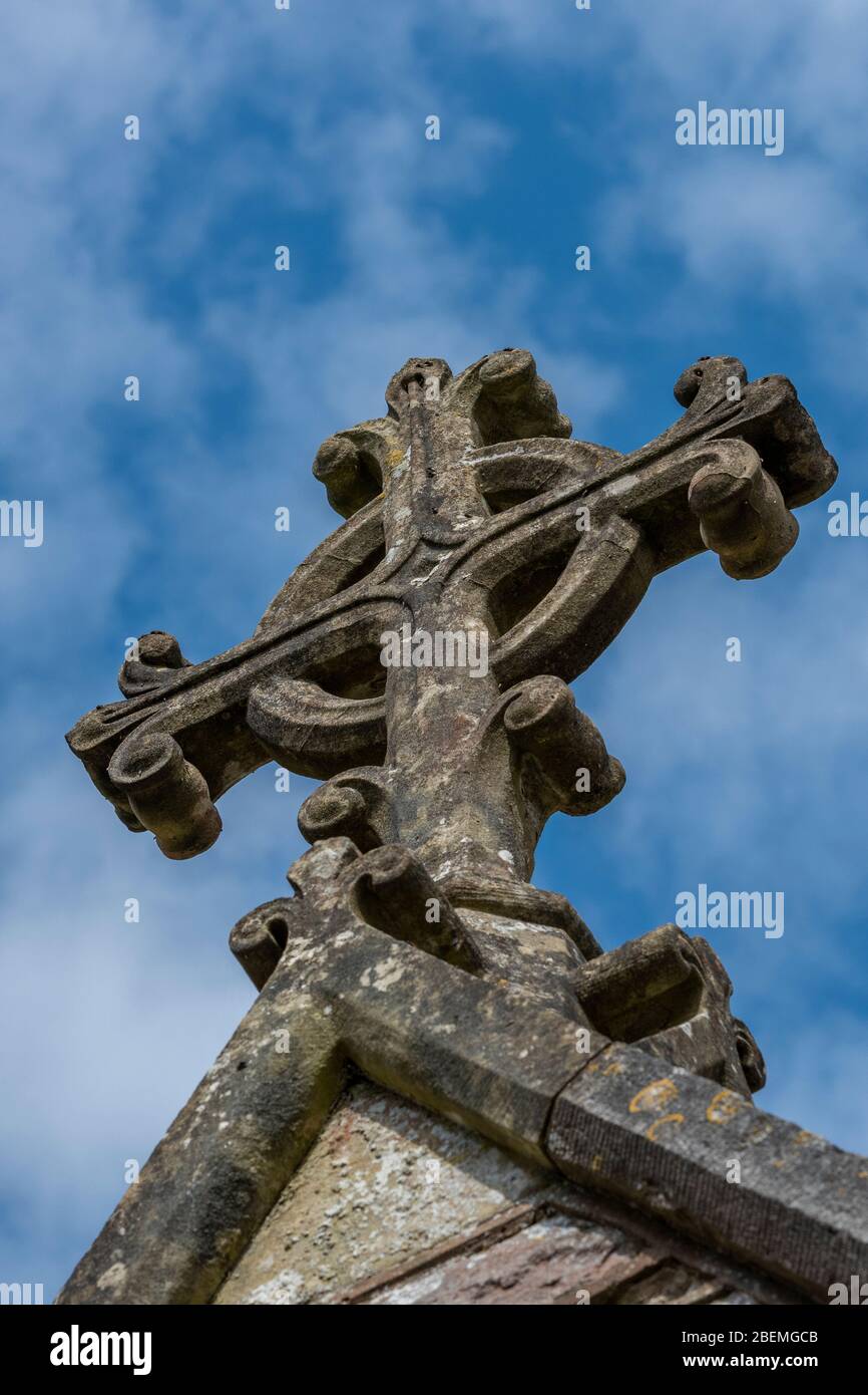 a Gothic inspired stone cross on the apex of a church roof set against ...