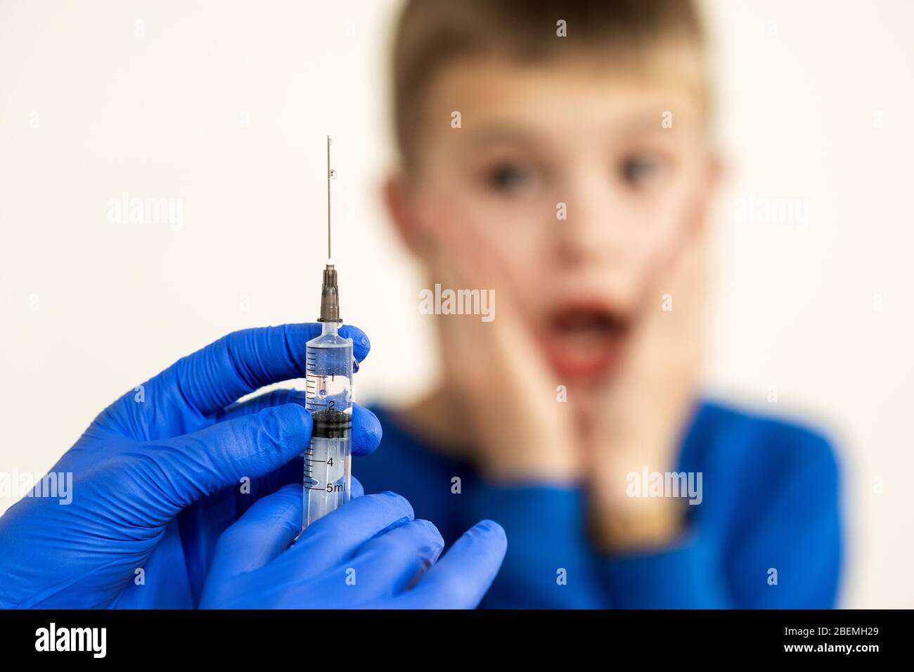 Doctor preparing vaccination injection with a syringe to an afraid ...