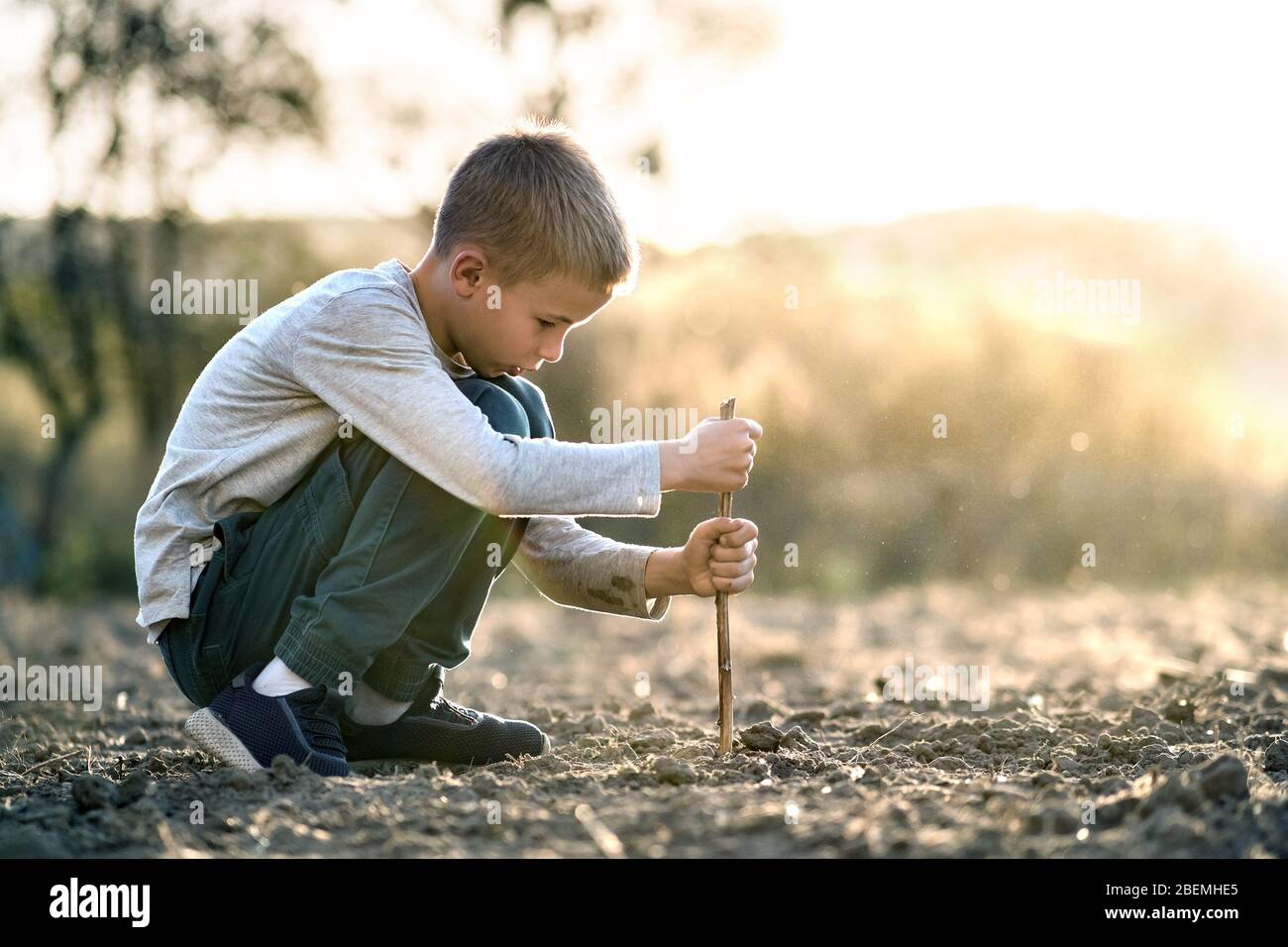 Child boy playing with wooden stick digging in black dirt ground ...