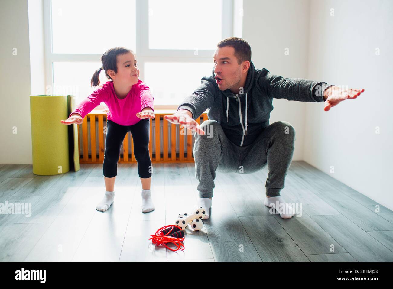 young father and his cute little daughter are doing squat exercises ...