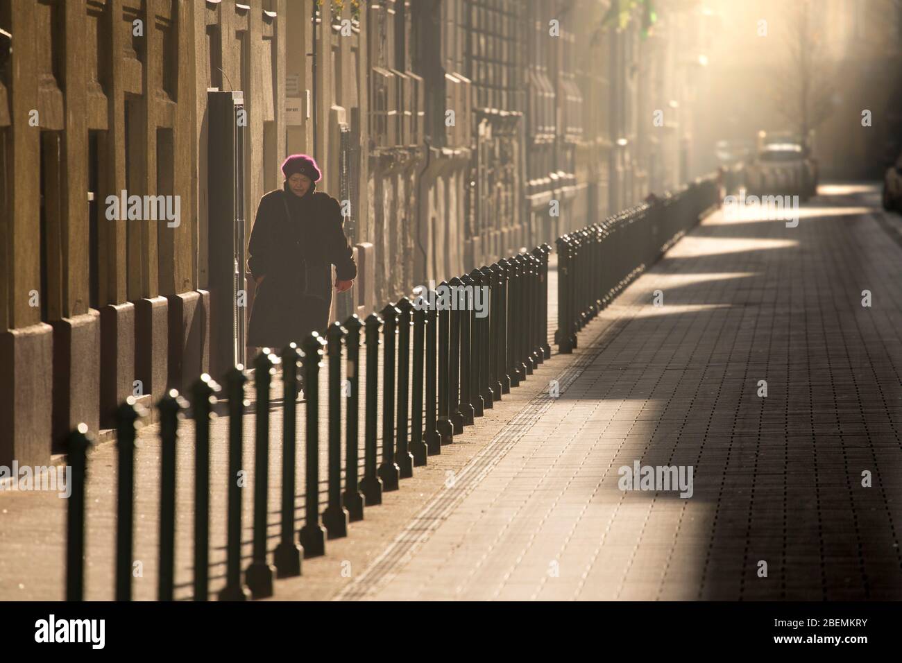 A female pedestrian walking on a sidewalk in the early morning light ...