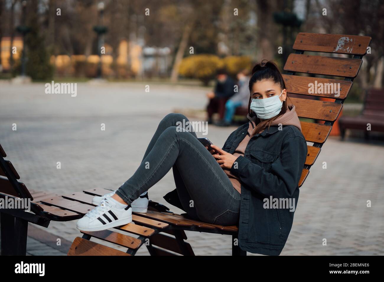 Yong woman sitting on the bench in the park and wearing a protective ...
