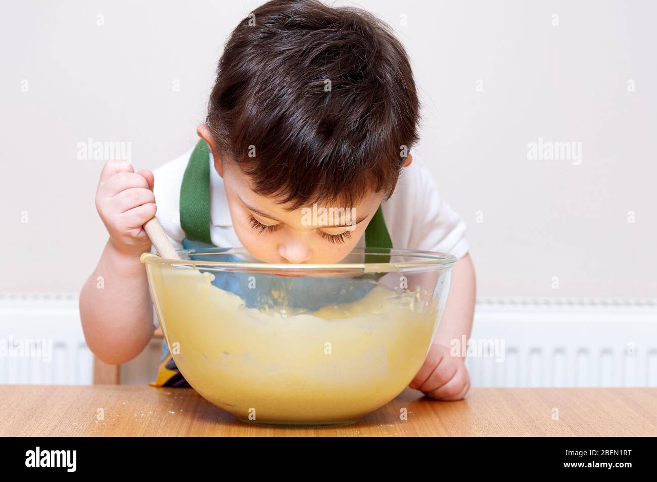 Young boy stirring cake mix wearing white t-shirt and green apron in ...