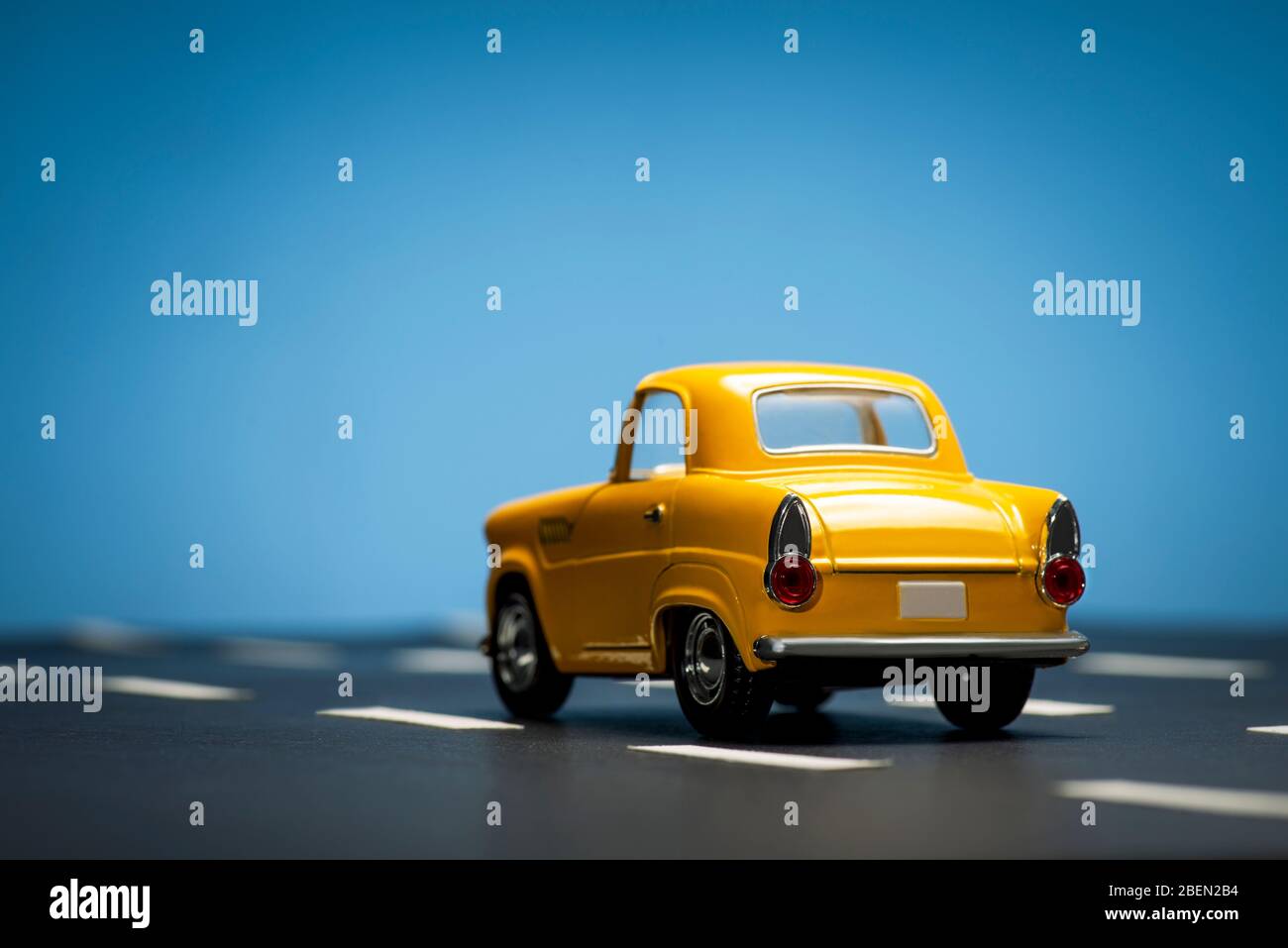 Rear view of a Yellow toy car on a blue background and on an asphalt ...