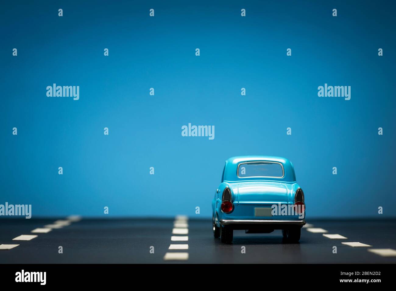 Rear view of a blue toy car on a blue background and on an asphalt road ...