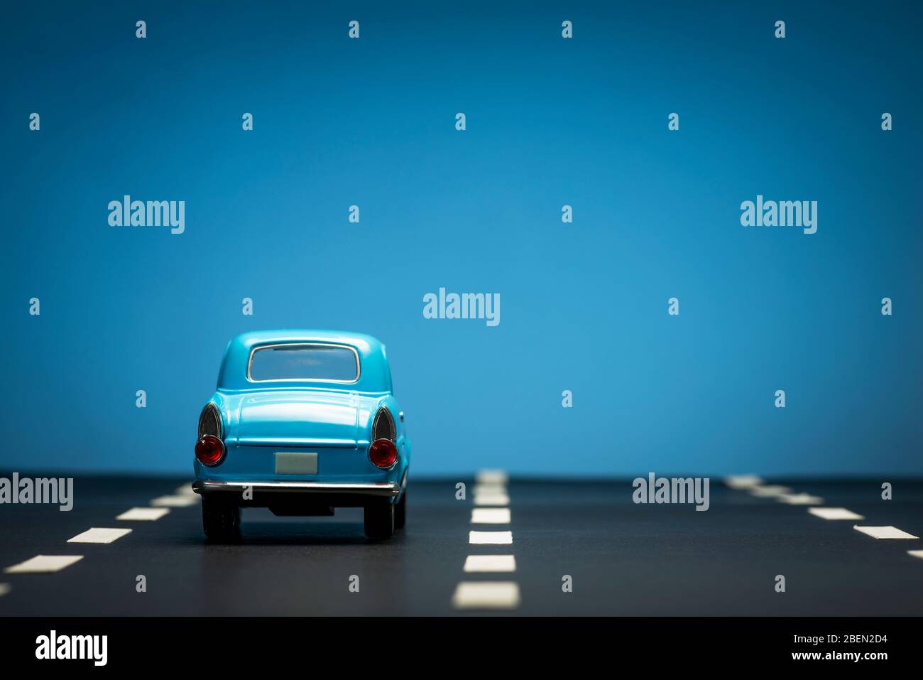 Rear view of a blue toy car on a blue background and on an asphalt road ...