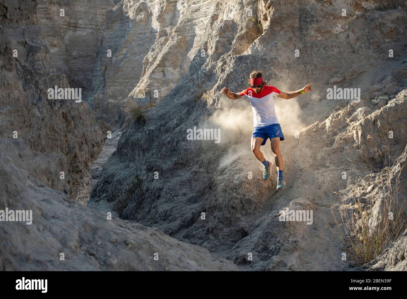 A man trail running down on technical terrain leaving dust on his way ...