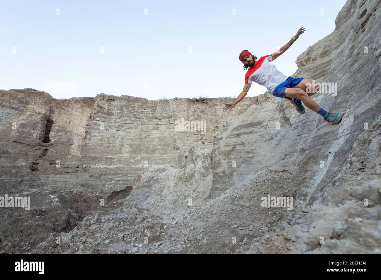 One man preforms a "wall ride" while trail running on a sandy terrain ...