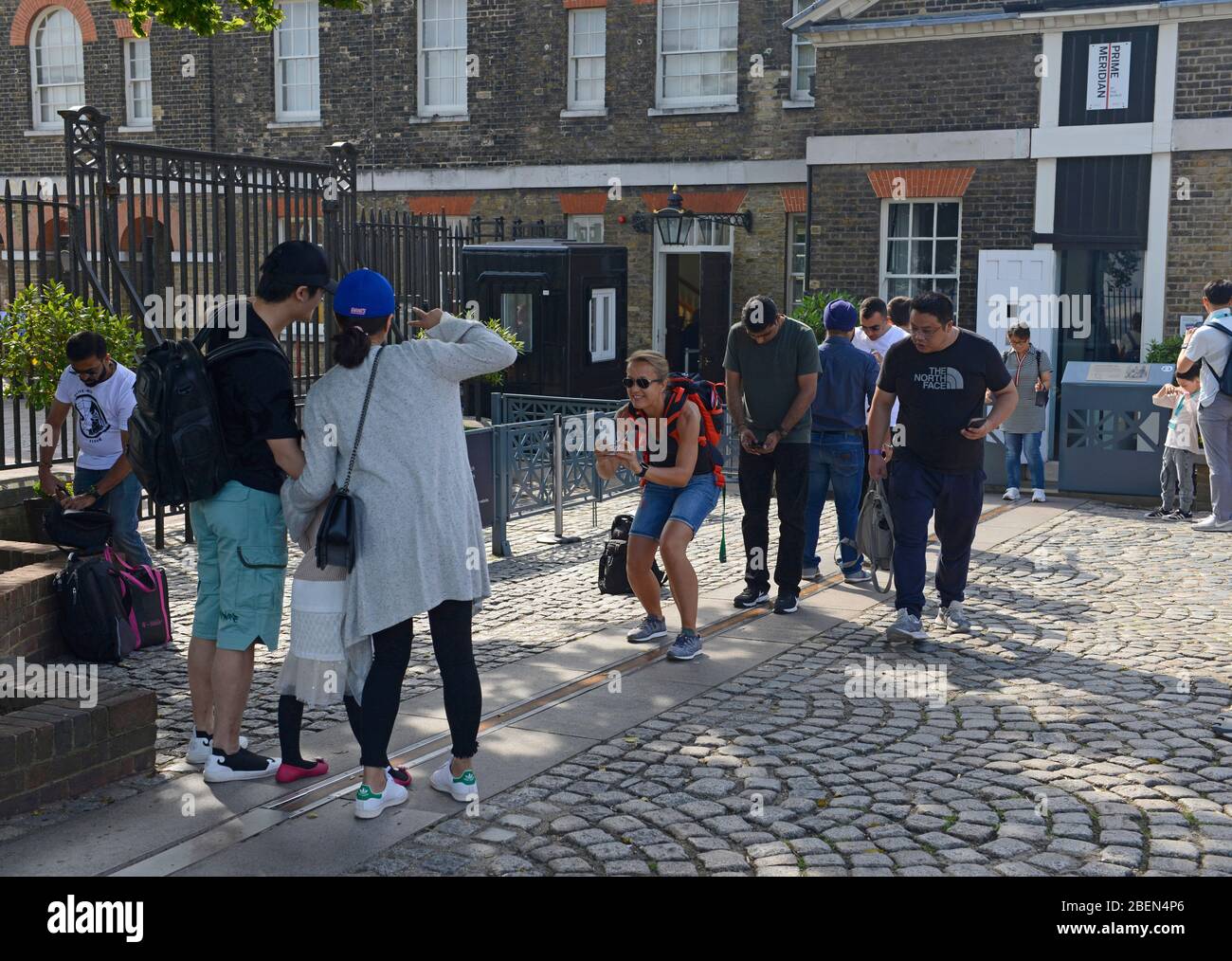 A visitor takes a photo of a family standing on the Greenwich Meridian ...