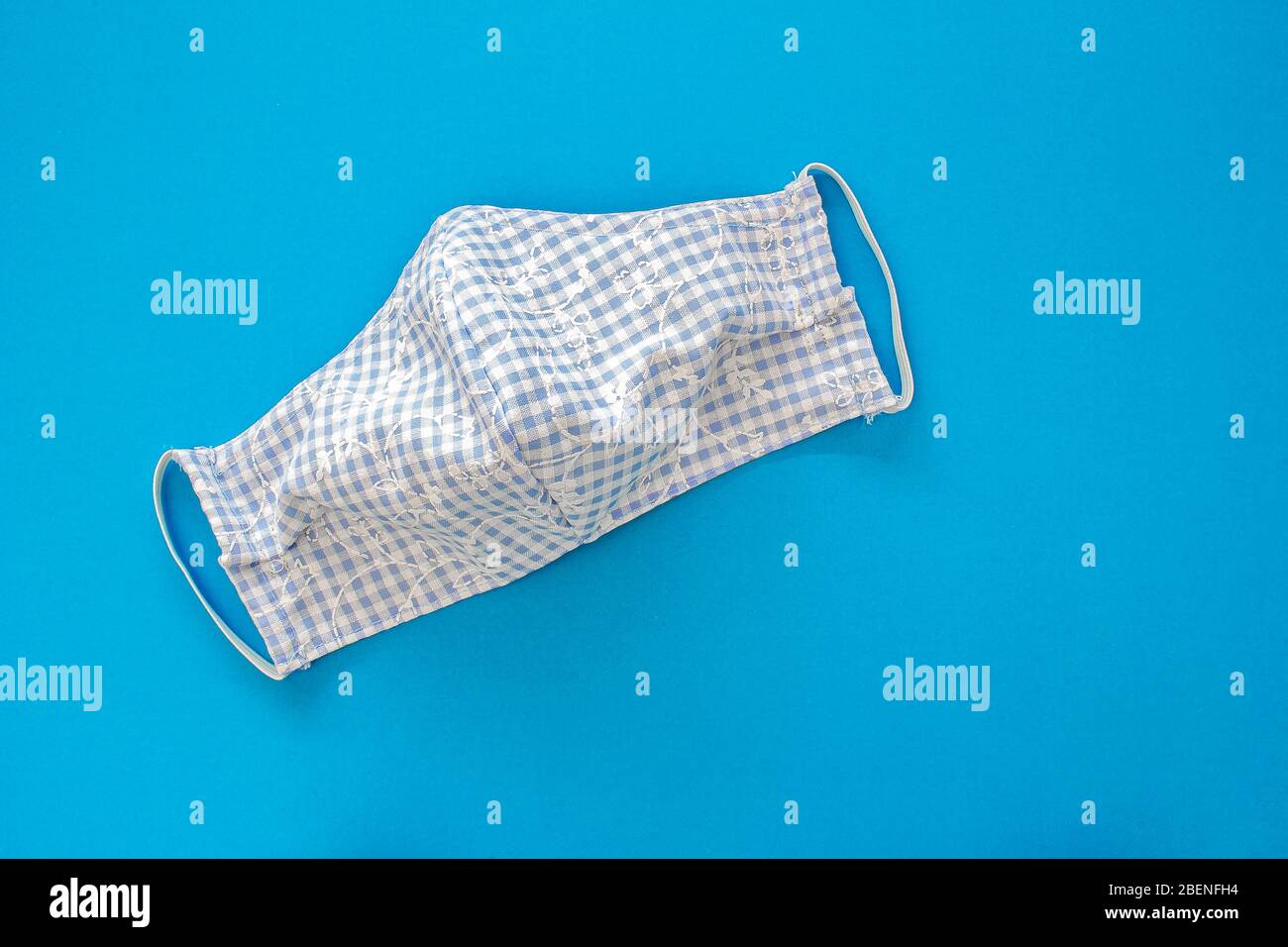 Blue and white checkered square homemade face mask for adults on a blue ...