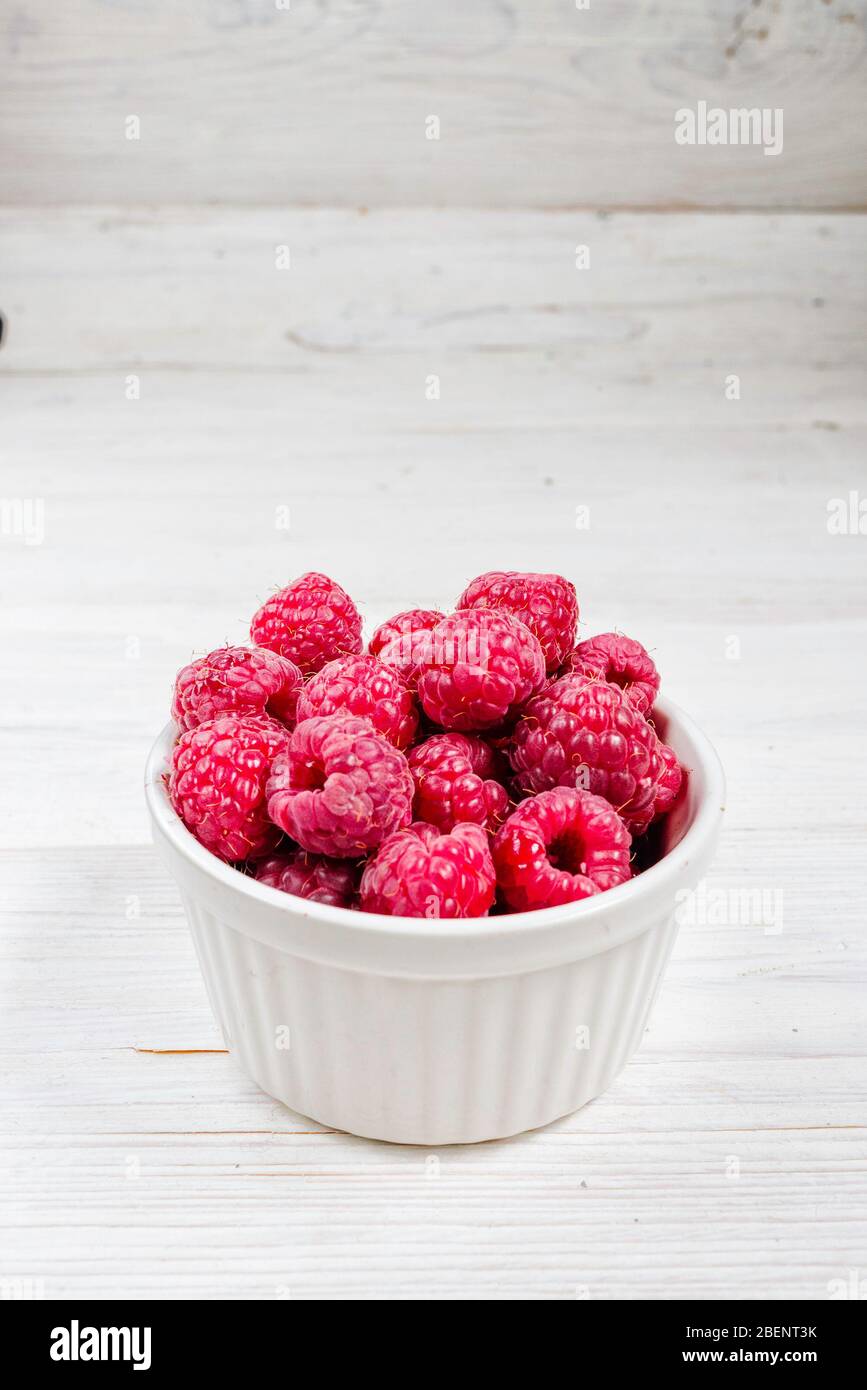 Raspberry in a white ceramic bowl over white wooden rustic background ...