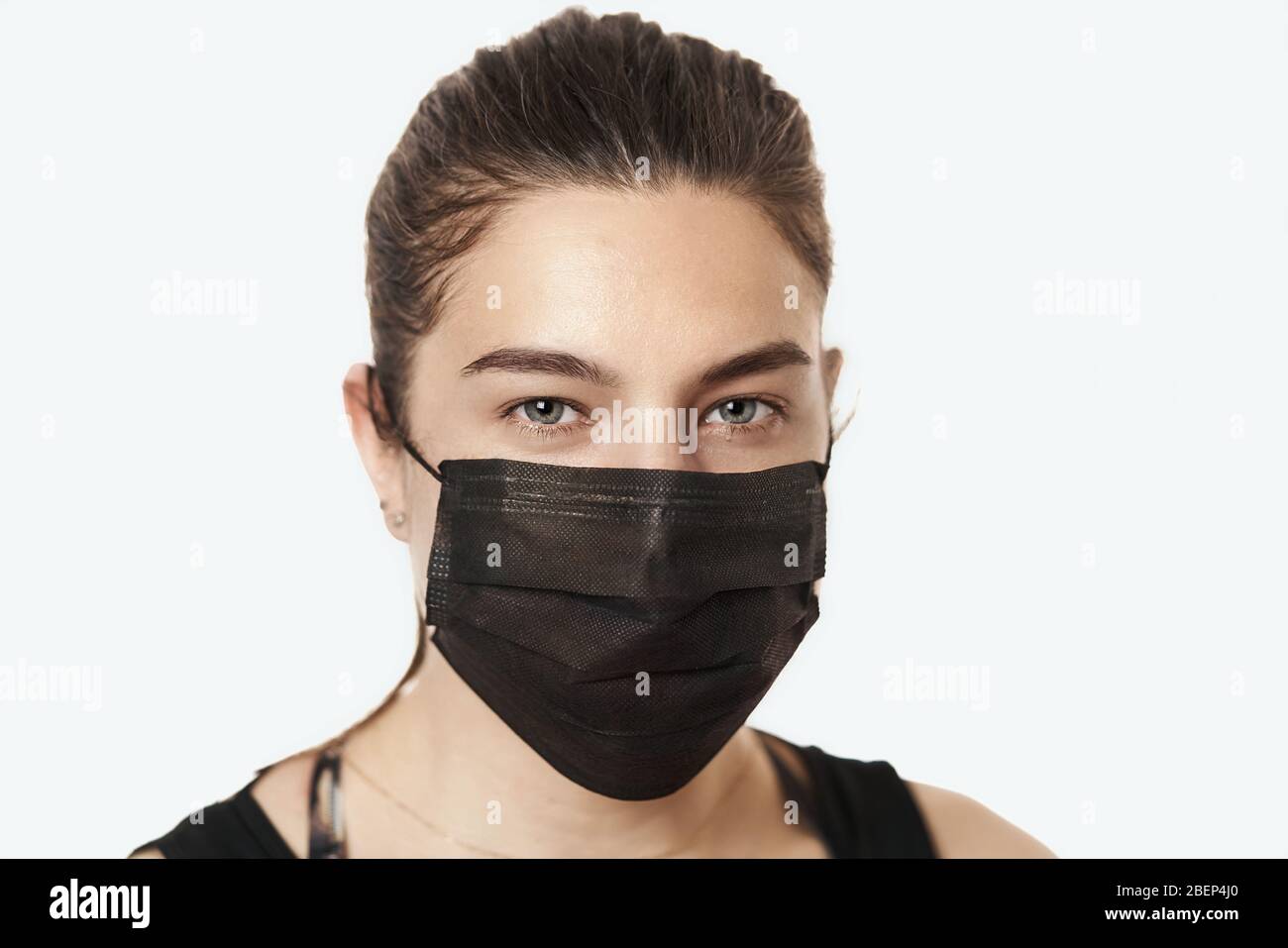 A close-up portrait of a pretty female wearing a surgical mask isolated ...