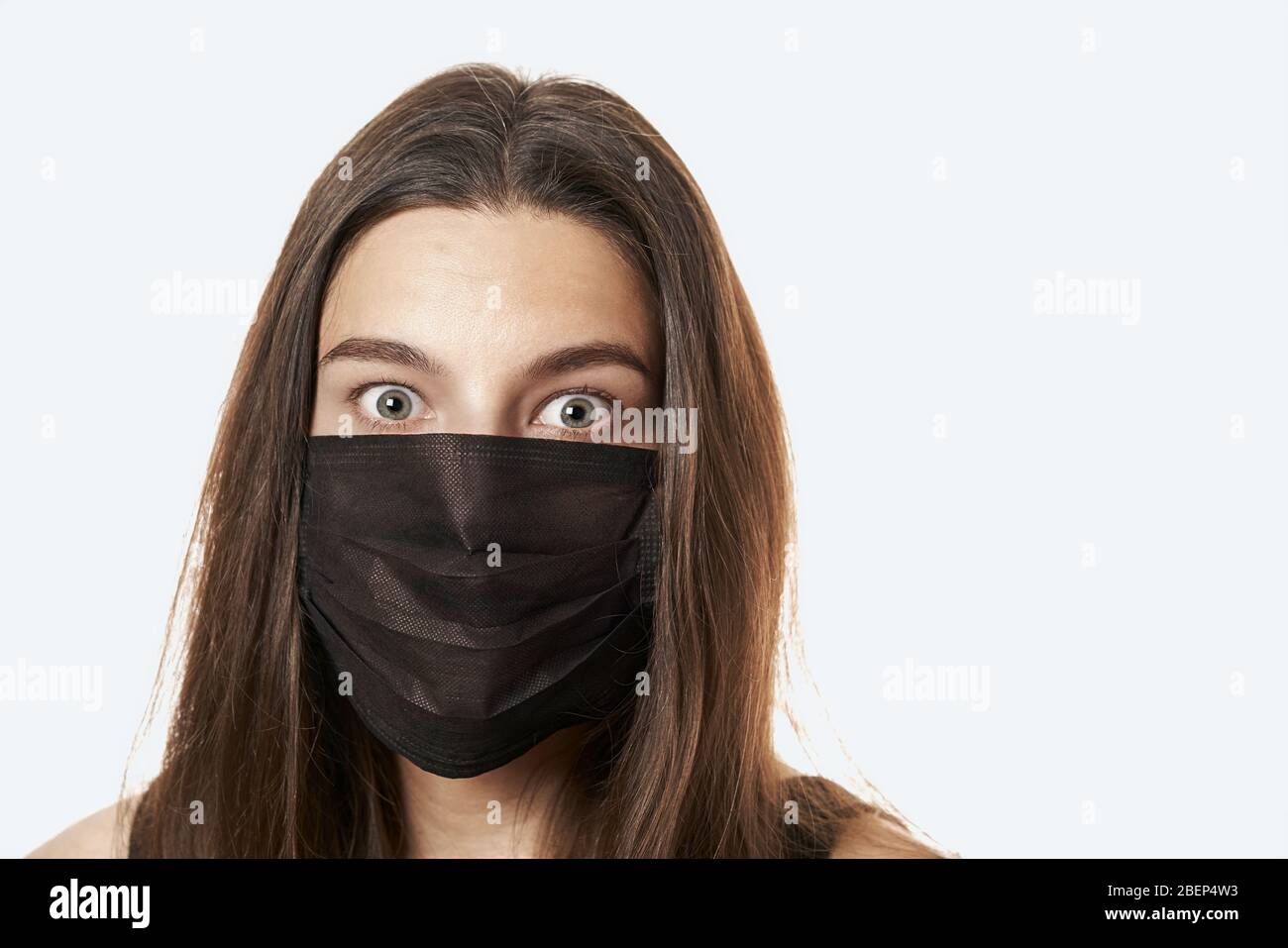 A close-up portrait of a pretty female wearing a surgical mask isolated ...