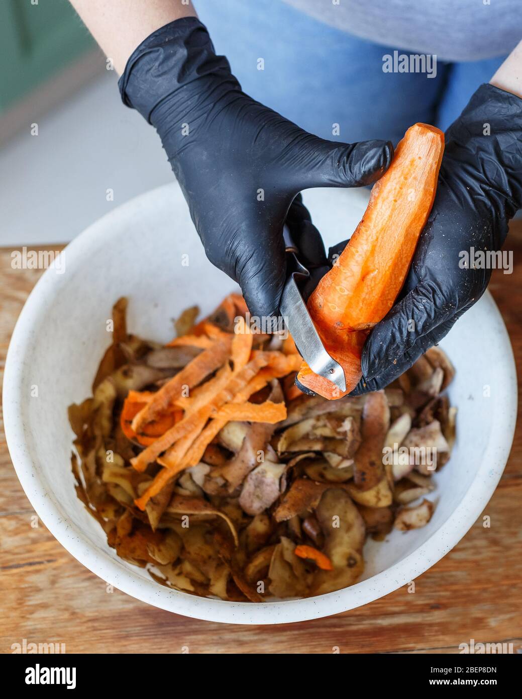 Woman peels a carrot into a bowl gathering vegetable scraps for compost ...