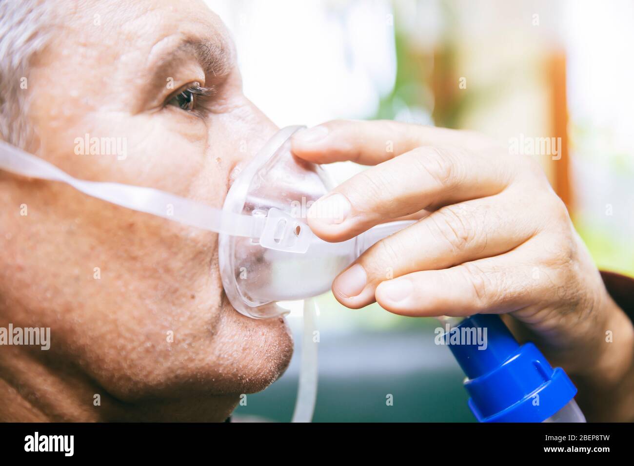 Senior man using medical equipment for inhalation with respiratory mask ...