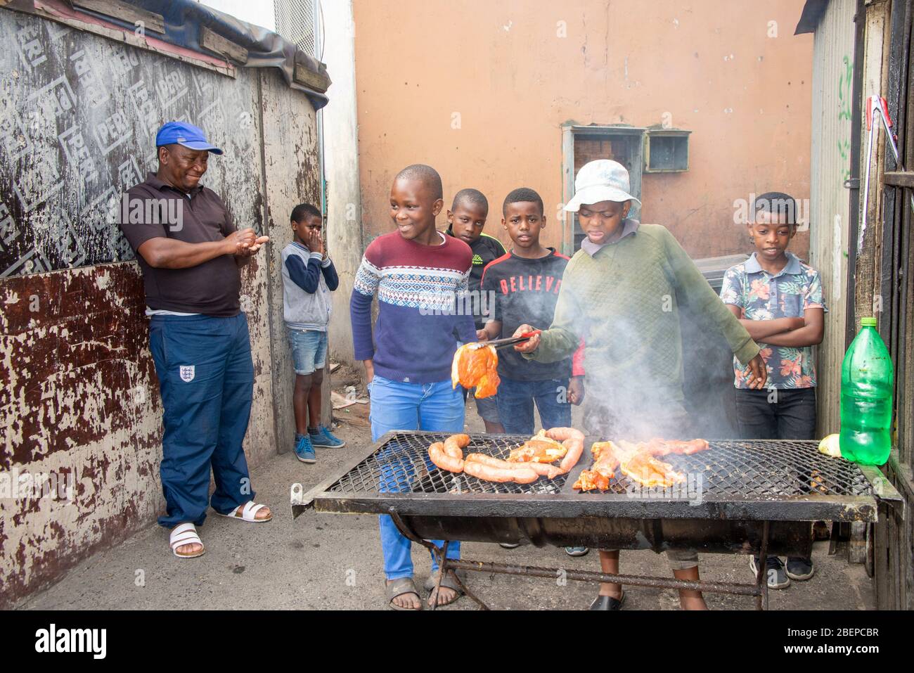 Boys cook meat on a grill in the side alley of a township in Cape Town ...