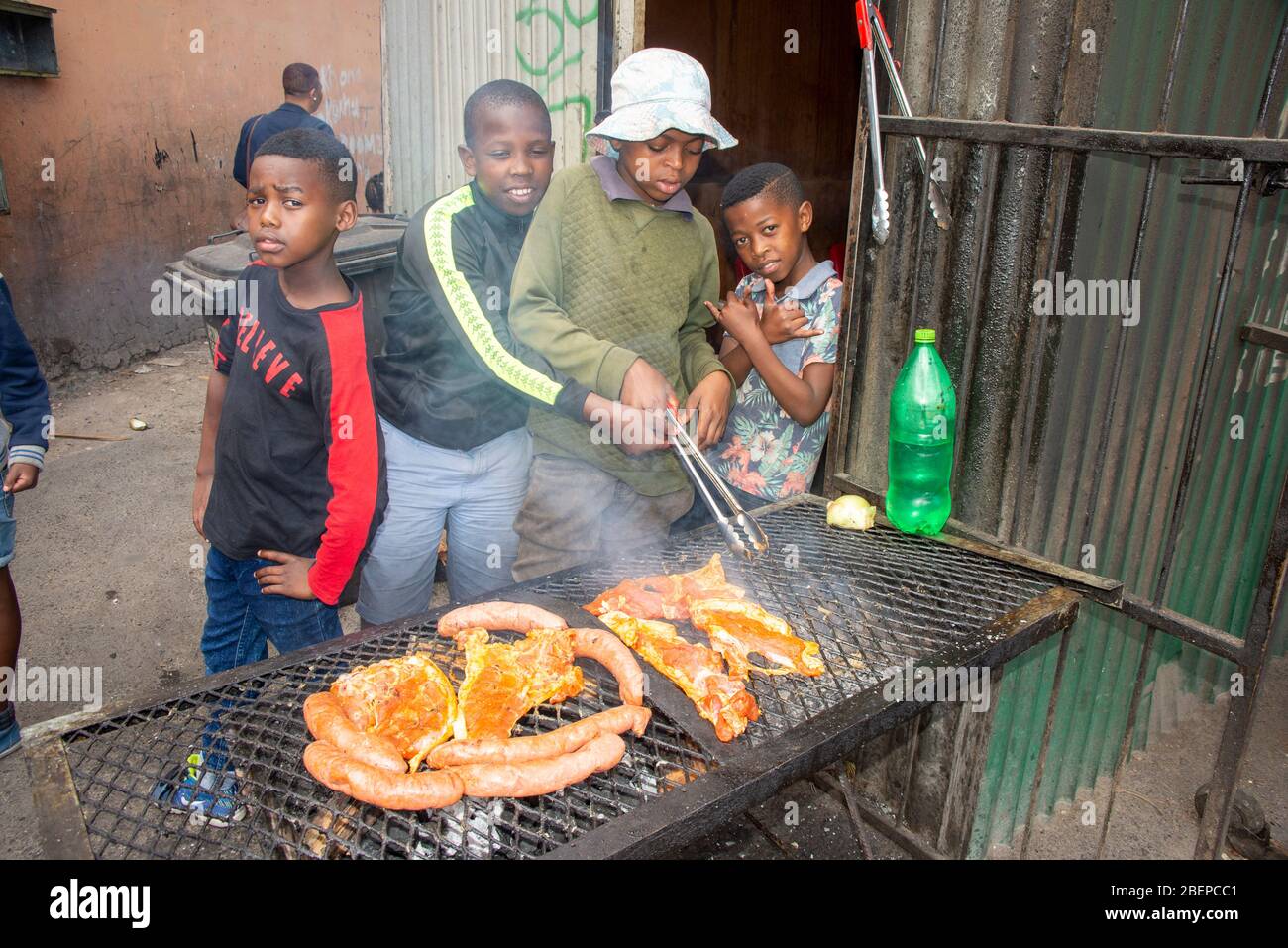 Boys cook meat on a grill in the side alley of a township in Cape Town ...