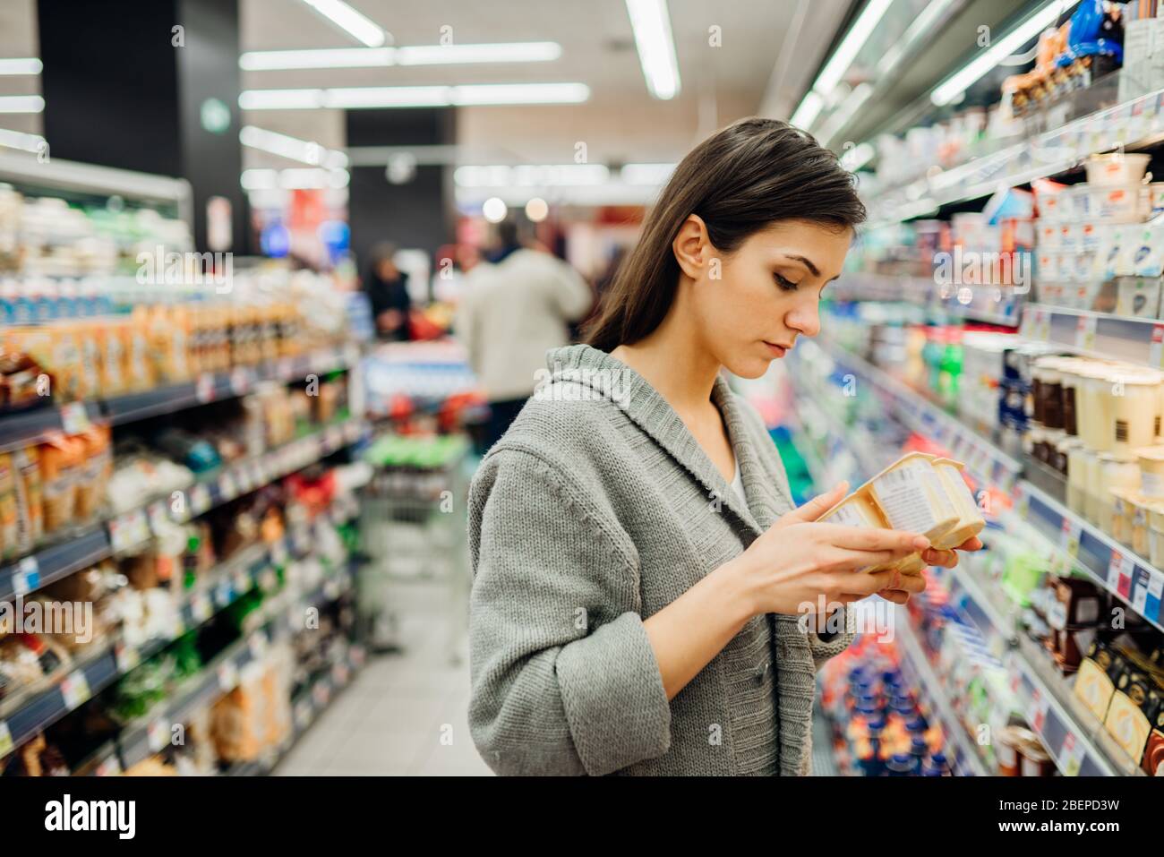 Woman shopping a dairy product in the supermarket grocery store.Reading ...