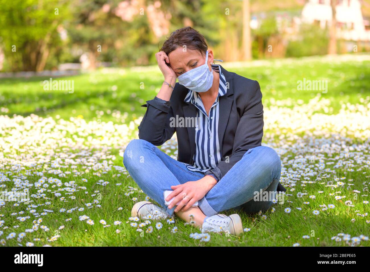 Worried woman wearing a face mask outdoors as she relaxes on the grass ...