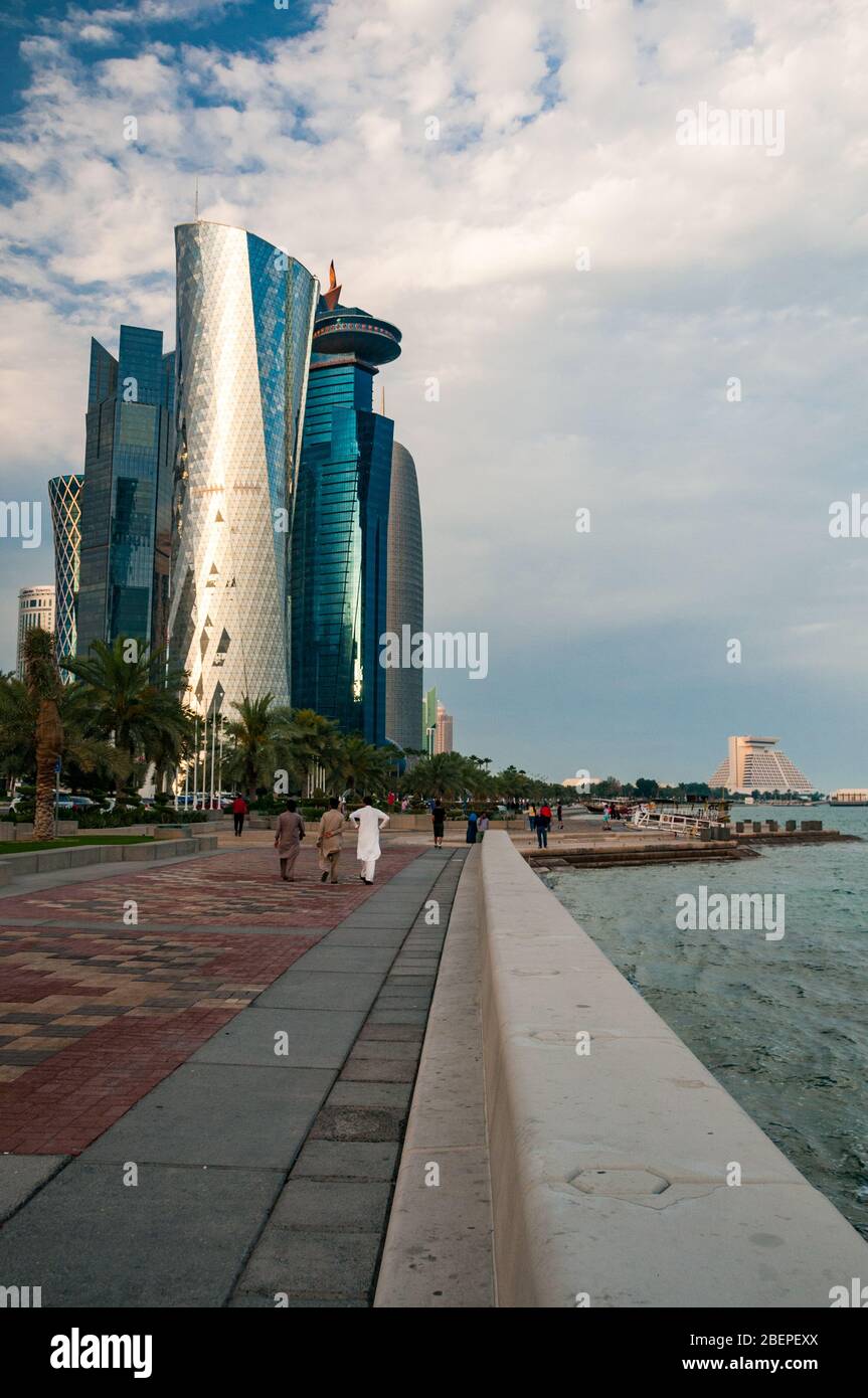 People walk along Al Corniche with the Doha Tower and modern buildings ...