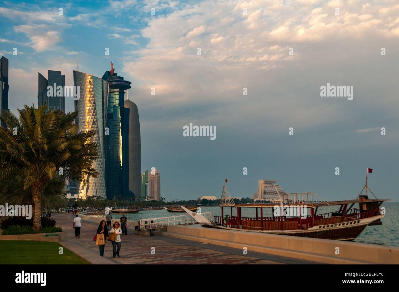 People walk past a dhow on Al Corniche with the Doha Tower and modern ...